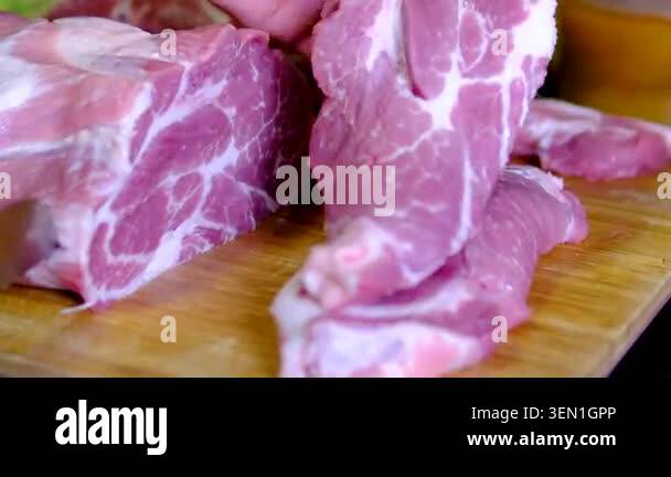 Fresh pork neck is cut into even steaks on a wooden board as male hands ...