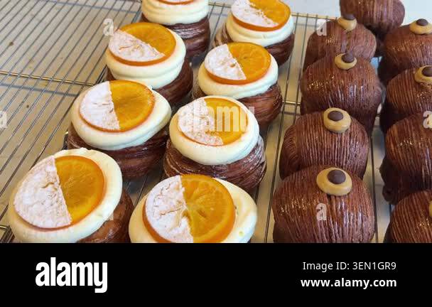 Delicate pastries topped with white cream and fresh orange slices stand ...