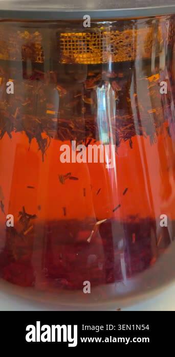 A transparent teapot reveals a deep amber tea with warm orange tones ...