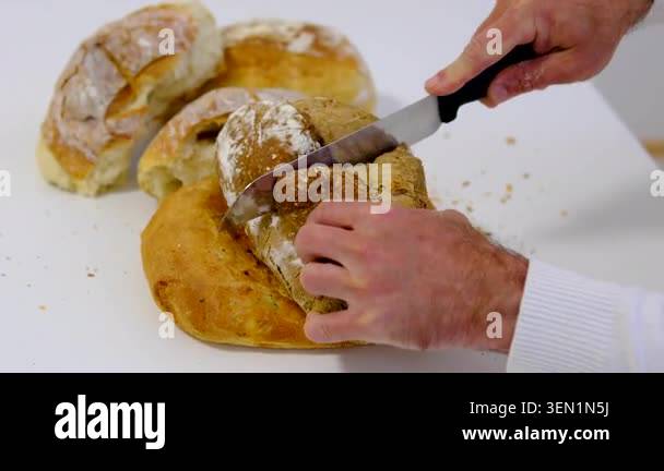 A freshly baked dark bread loaf is cut open by male hands revealing a ...