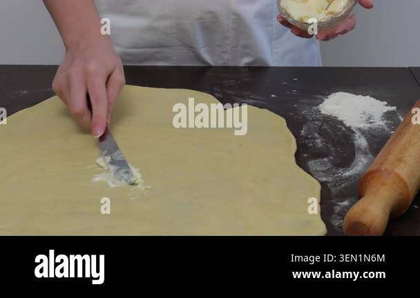 A woman carefully spreads a layer of softened butter across smooth ...