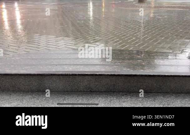 Large raindrops strike wet asphalt creating countless splashes while ...