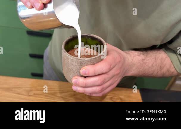 Male hands mixing cocoa powder with warm milk in gray green ceramic mug ...