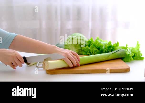Female hands cutting leek with large knife on wooden board beside ...