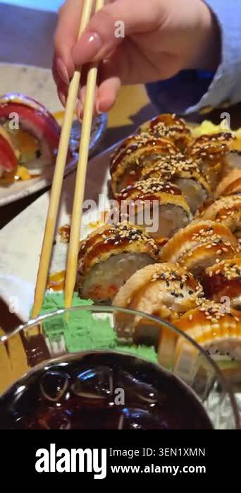 A diner carefully picks up green wasabi with disposable chopsticks and ...