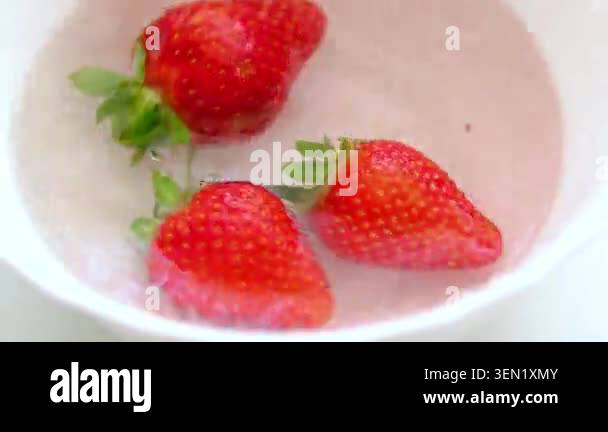 Large ripe strawberries floating in white bowl filled with water while ...