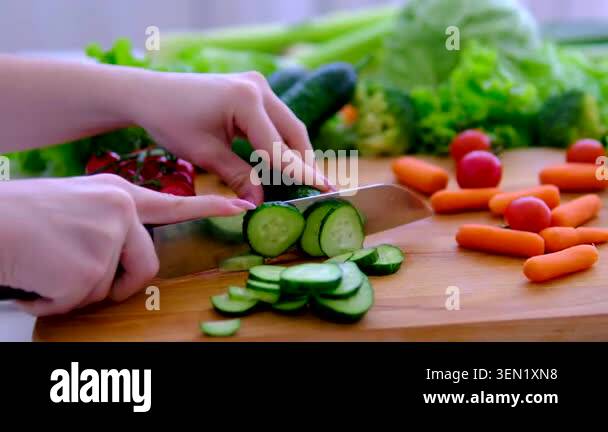 Female hands cutting crunchy cucumber into thin round slices on rustic ...