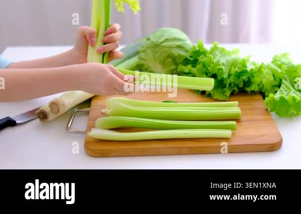 Female hands snapping crunchy celery stalks on rustic wooden board ...