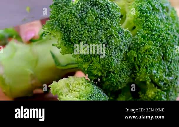 Fresh broccoli heads separated into pieces with large knife on wooden ...