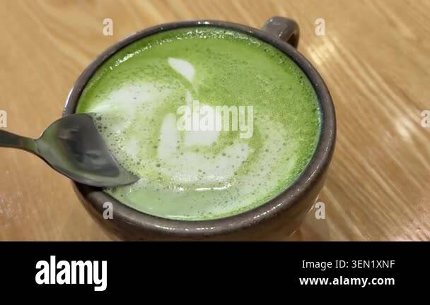 Teaspoon lifting soft creamy foam from green matcha latte creating rich ...