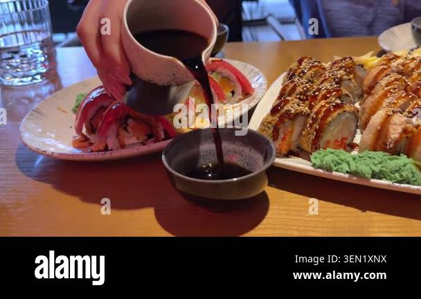 Dark soy sauce streams into small dipping dish while fresh sushi rolls ...