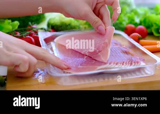Woman opening prosciutto packaging and lifting soft meat ribbons beside ...