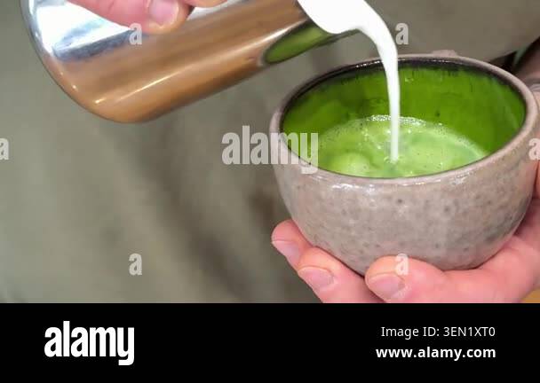 Male hands slowly pour milk into vibrant green matcha tea creating ...