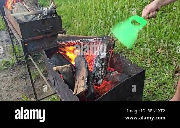Bright flames rise from stacked firewood inside a metal grill as people ...