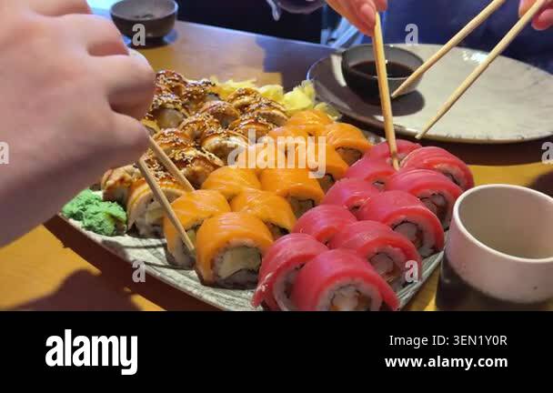 Four people reach for sushi rolls at the same time using wooden ...
