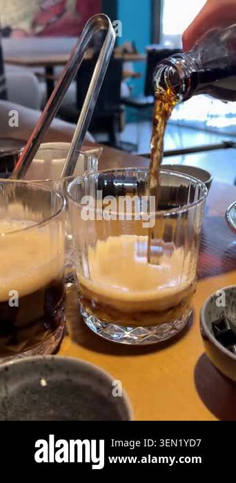 Dark sparkling cola poured into clear glass on wooden restaurant table ...