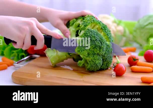Female hands chopping broccoli pieces on wooden board beside fresh ...