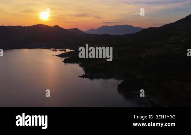 Aerial drone view over a calm lake reflecting golden light, surrounded ...