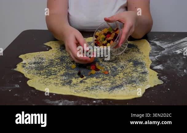 A young woman sprinkles sweet raisins and colorful dried fruits over a ...