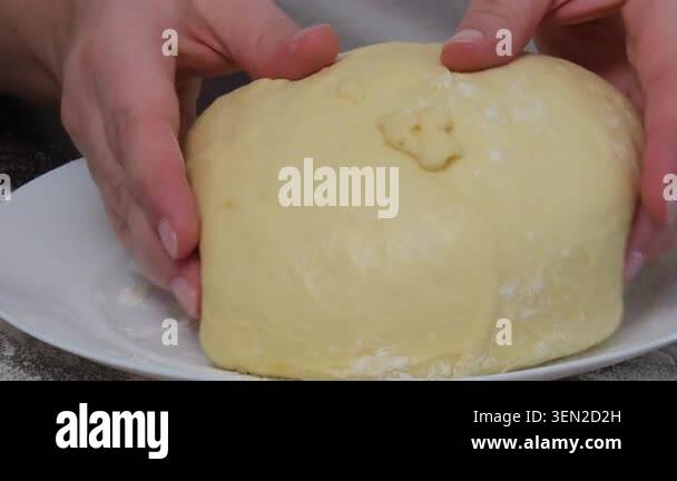 A woman transfers freshly risen yeast dough onto the work surface. A ...