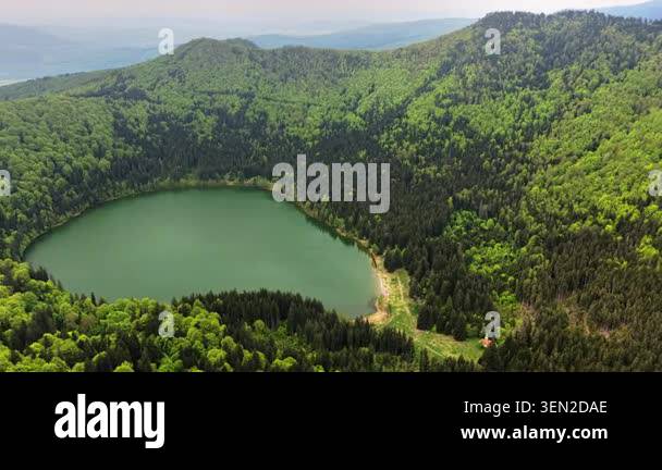 High-altitude aerial view of a round crater lake encircled by forest ...