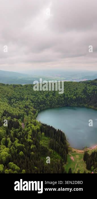 High-altitude aerial view of a round crater lake in a forest bowl above ...