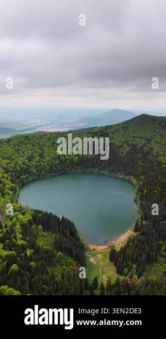 High-altitude aerial view of a round crater lake ringed by forest above ...