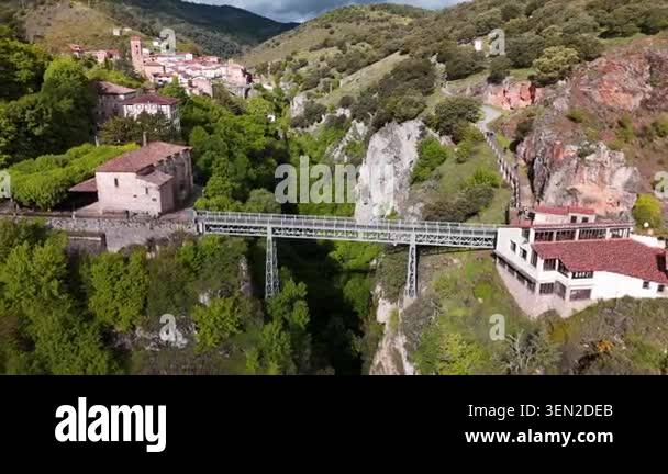 Aerial panoramic view of a metal footbridge and historic stone church ...