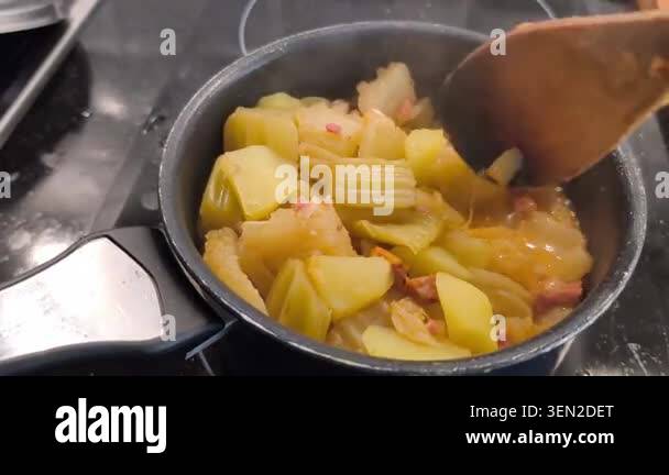 Close up of a person stirring a steaming cardoon and potato stew with a ...