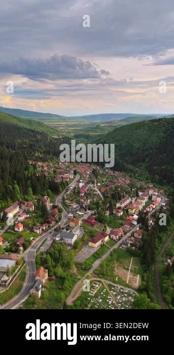 Aerial drone view of a mountain town in a forested valley with a plain ...