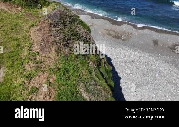 Aerial panoramic reveal shot of a wild pebble beach and rocky cape with ...