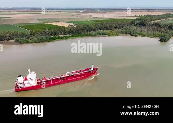 High angle drone perspective following a red cargo ship. The industrial ...