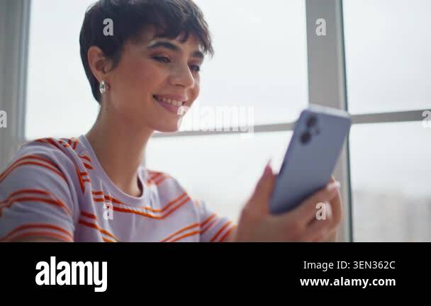 Smiling student texting mobile phone sitting panoramic window closeup ...