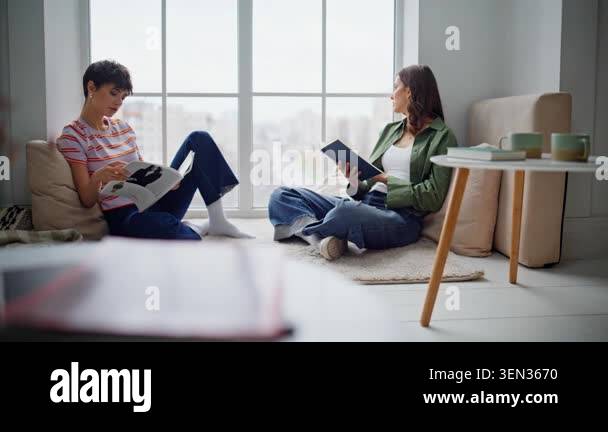 Relaxed two readers sitting light apartment floor by panoramic window ...