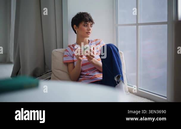 Serene woman enjoying drink sitting by window looking city view. Happy ...