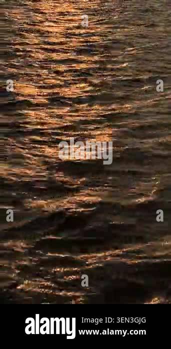 Golden sunset reflects over the abstract ripples and dark blue waves of ...