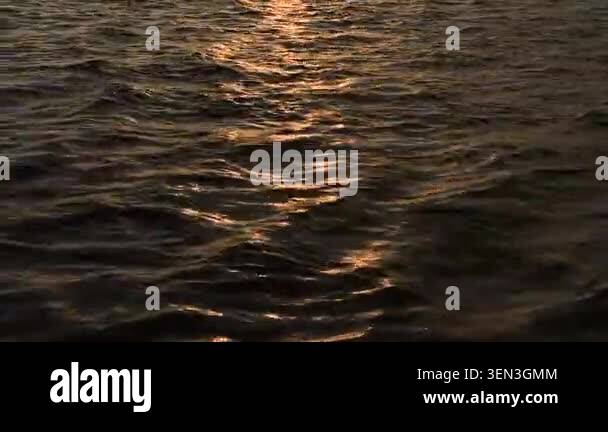 Golden sunset reflects over the abstract ripples and dark blue waves of ...