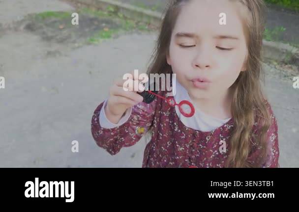 A cheerful little girl playing outdoors and blowing soap bubbles Stock ...