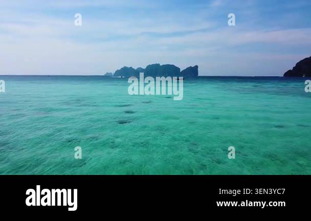 Aerial view flying over crystal clear turquoise water towards the ...