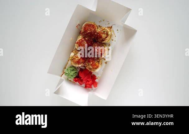 Womans hand picking up a hot baked sushi roll from a takeaway paper box ...