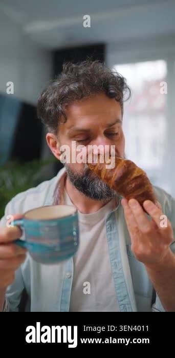 Happy caucasian man enjoying a fresh croissant and coffee for breakfast ...