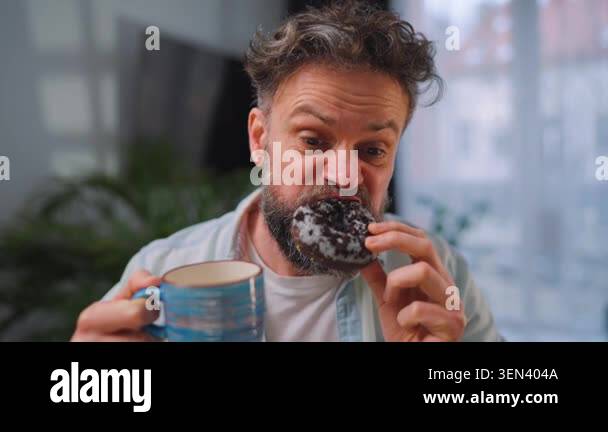 Sweet addiction concept. A man eats a donut and drinks coffee with ...