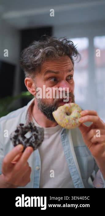 Guilty pleasure. A man eating two donuts simultaneously with delight ...