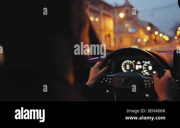 Backseat view on man driving car through bustling city at dusk under ...