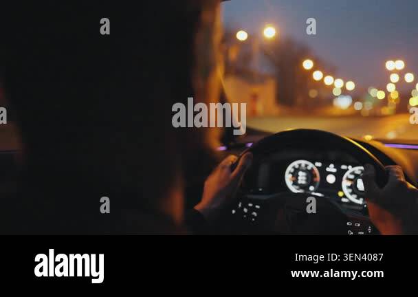 Backseat view on man driving car through bustling city at dusk under ...