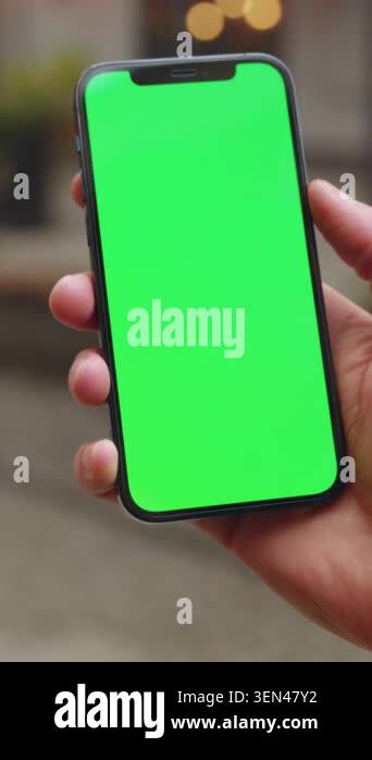 hand holding smartphone with green screen, thumb tapping home area near ...