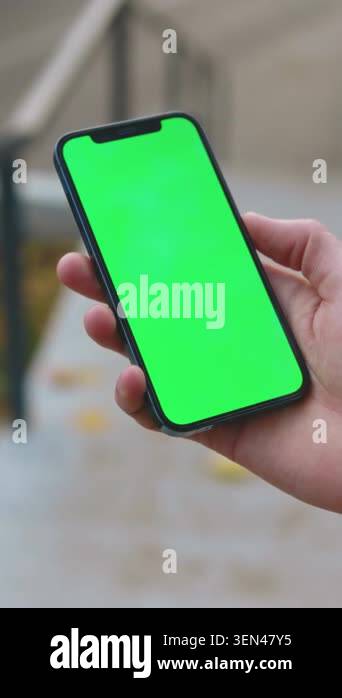 hand holding phone with green screen outdoors, closeup of thumb grip ...