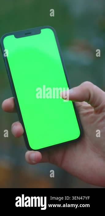 hand holding smartphone green screen in park, warm bokeh foliage ...