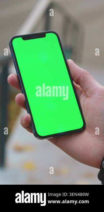 closeup of hand holding smartphone with green screen, stair railing and ...