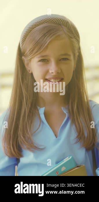 young caucasian girl holding books in sunny school corridor, wearing ...